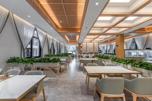 Uma sala de jantar moderna com mesas, cadeiras, plantas e teto com painéis de madeira e iluminação embutida.
