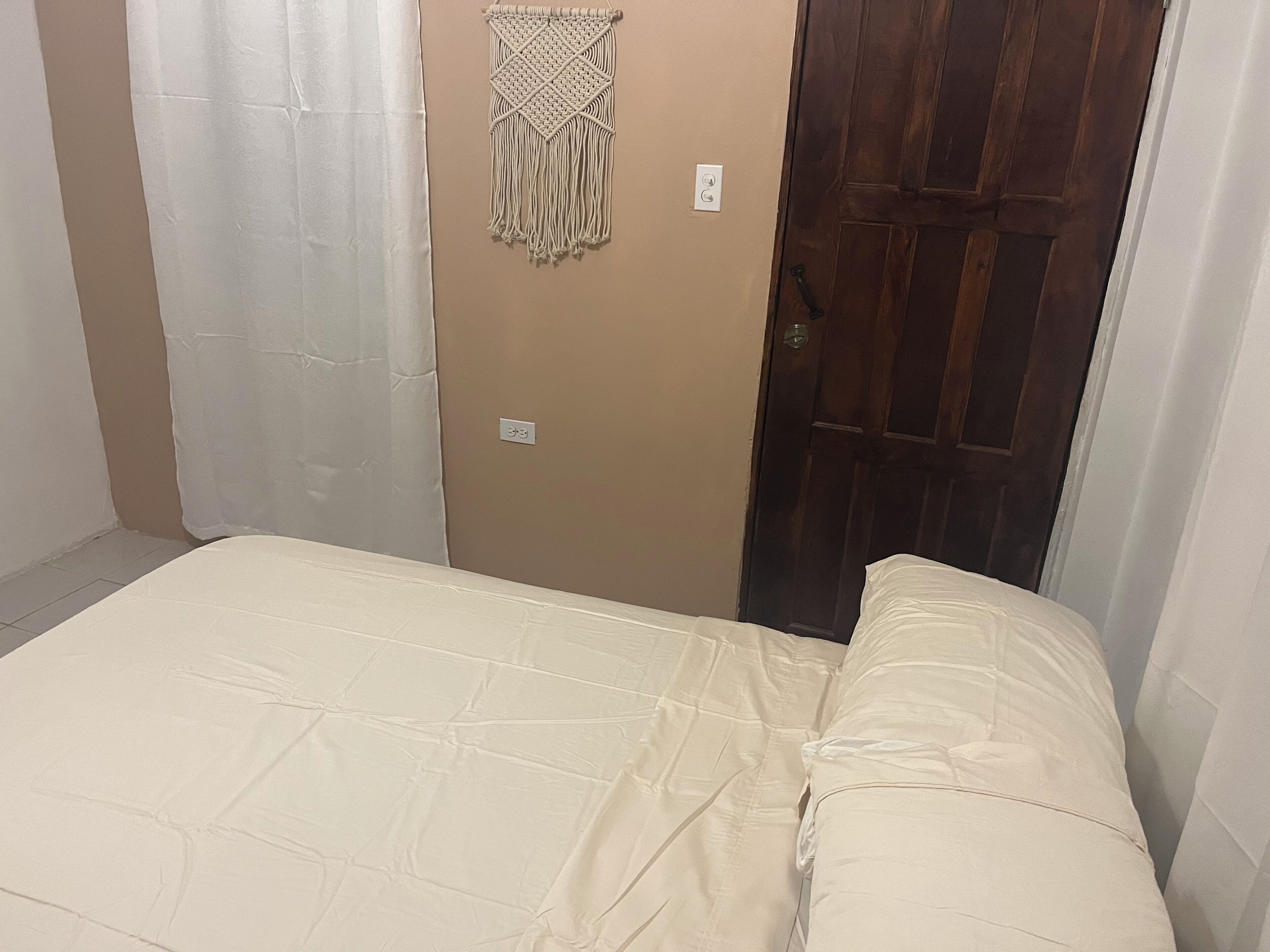 Quarto com cama, porta e um painel de macramé fixado na parede.