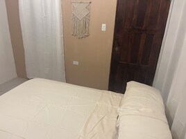 Quarto com cama, porta e um painel de macramé fixado na parede.