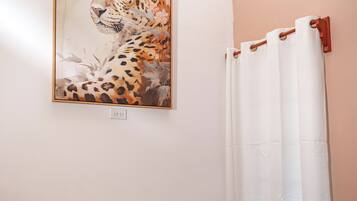 Quarto com cama, travesseiros, mesa de cabeceira com garrafas, abajur e pintura de um leopardo.