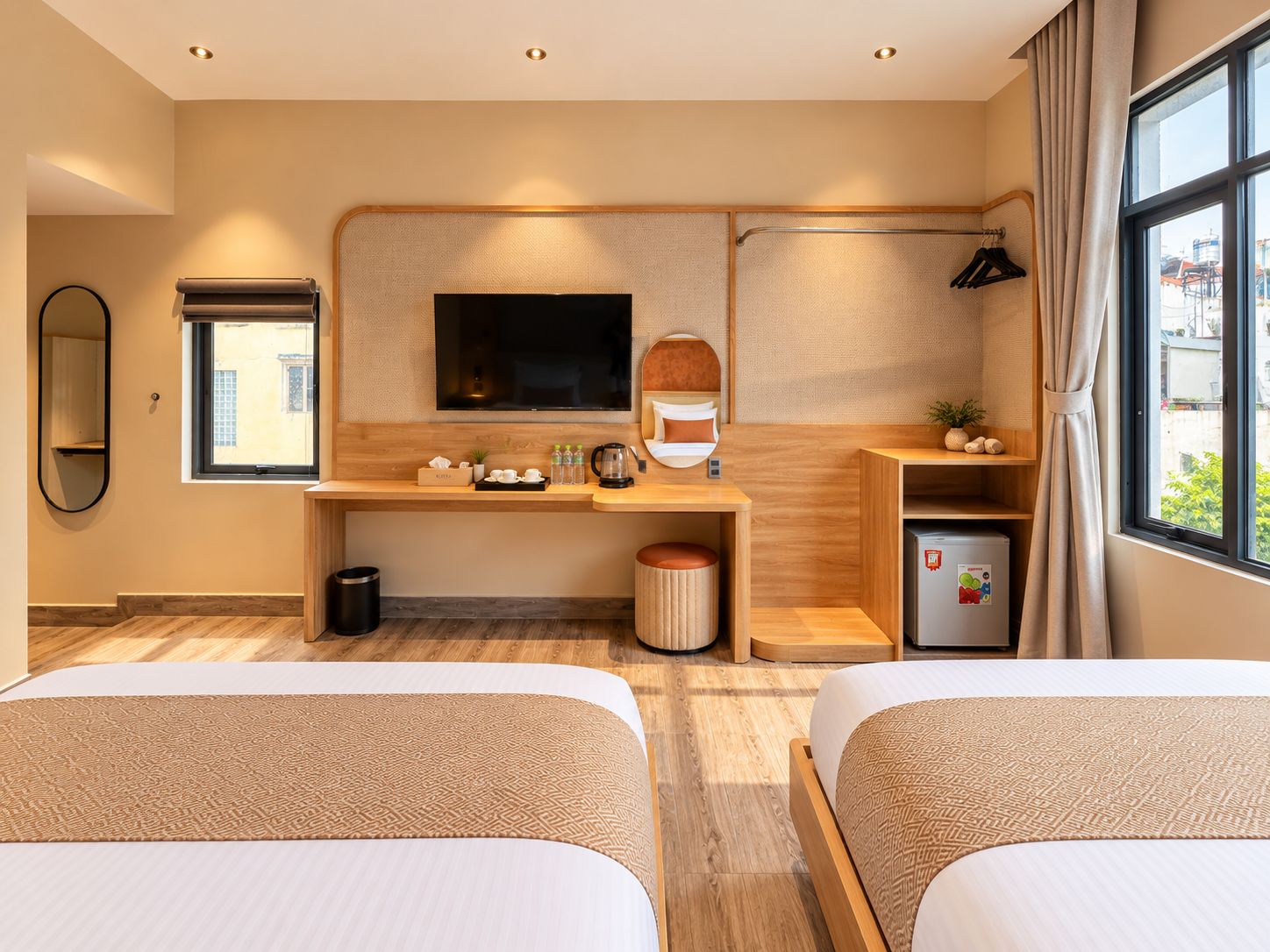 Quarto de hotel com duas camas, uma mesa de trabalho com televisão, mini-geladeira e janela com cortinas.