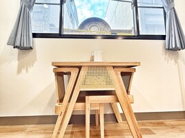 Uma mesa de madeira com uma cadeira de fibra natural em um quarto com janela.