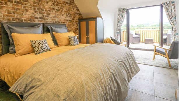 Quarto com parede de tijolos, uma cama grande com muitas almofadas, um guarda-roupa e uma varanda com móveis de exterior.