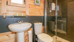 Casa de banho de uma cabana de madeira, com lavatório, sanita e cabine de chuveiro com vidro.