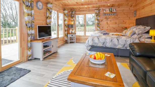 Interior acolhedor de uma cabana com teto de madeira, uma cama com roupa de cama estampada, uma televisão e uma área de jantar com uma fruteira.