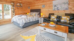 Interior acolhedor de uma cabana de madeira, com uma cama, um sofá, uma mesa de centro e um quadro na parede.