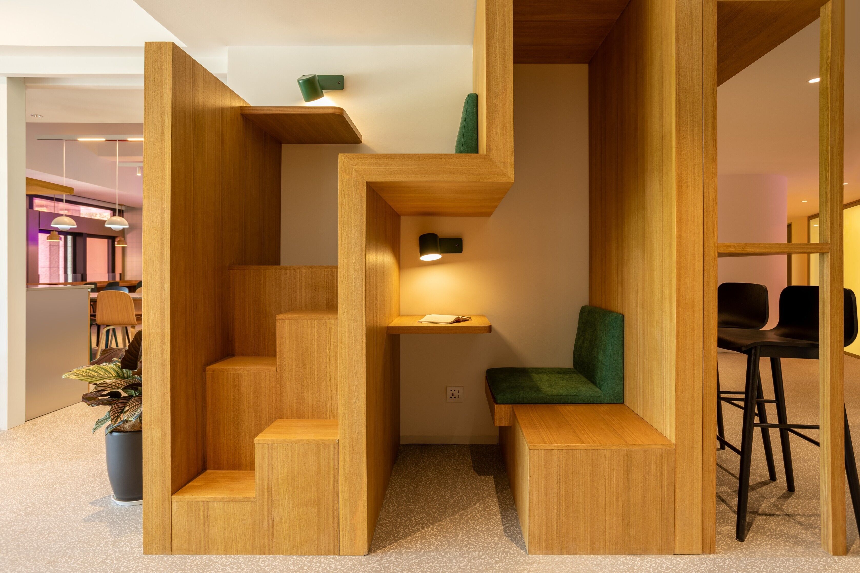 Interior moderno com escadarias de madeira, um banco acolchoado verde e uma pequena mesa com abajur.