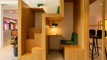 Interior moderno com escadarias de madeira, um banco acolchoado verde e uma pequena mesa com abajur.
