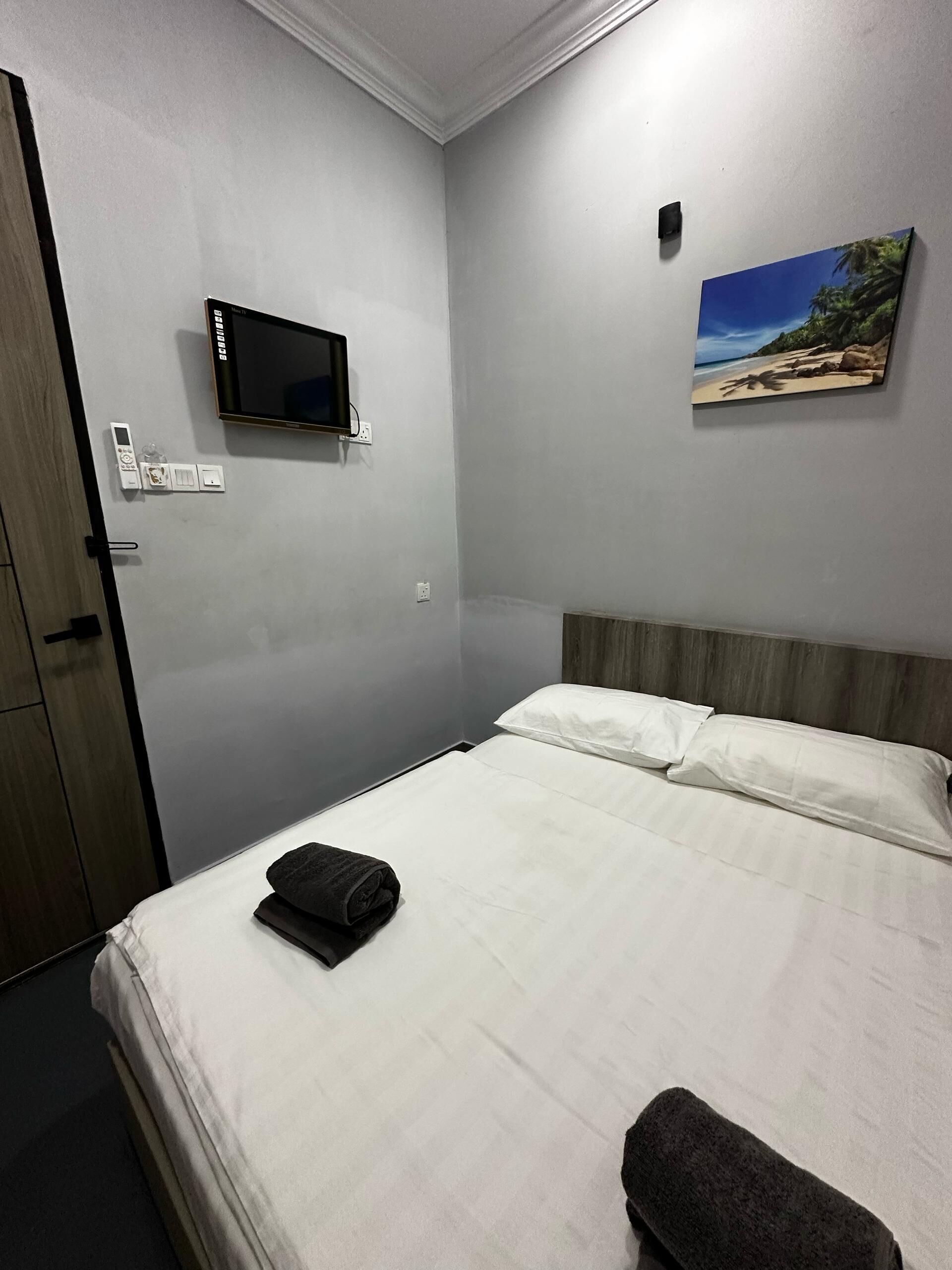 Quarto de hotel com uma cama, televisão fixada na parede, pintura de uma praia e um guarda-roupa de madeira.