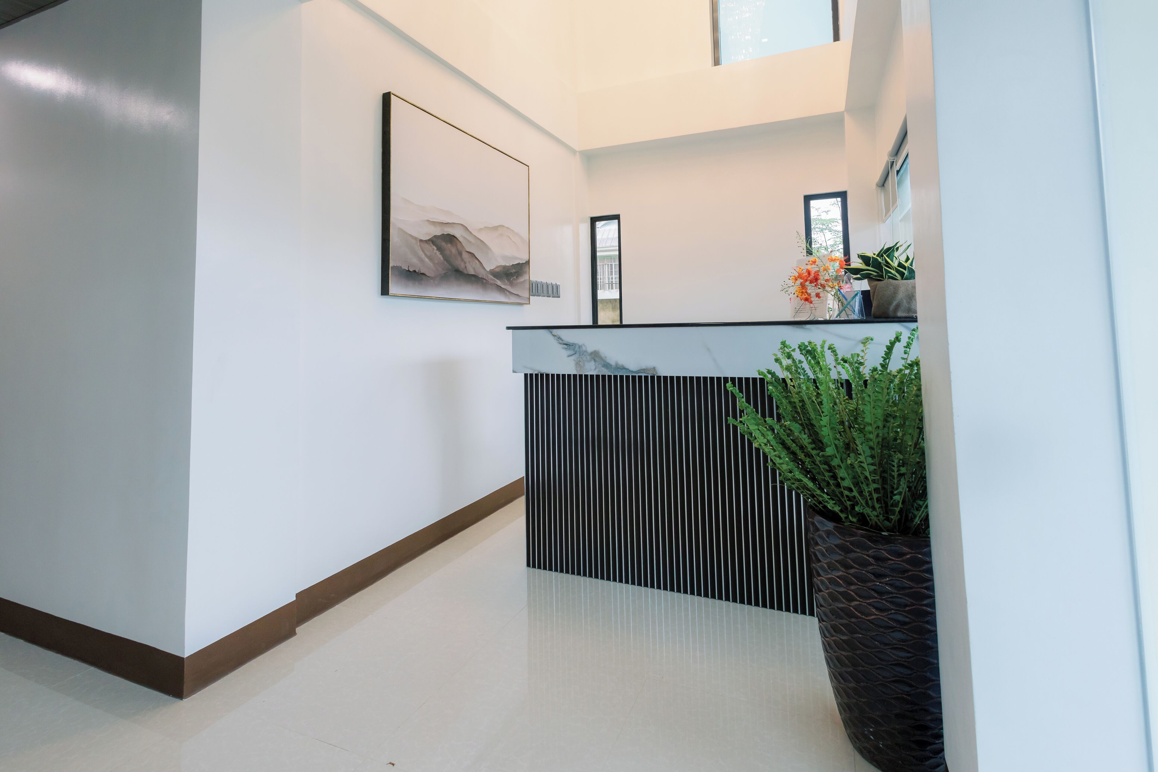 Uma área de recepção moderna com design minimalista, com um balcão de atendimento, uma obra de arte emoldurada e um vaso de planta.