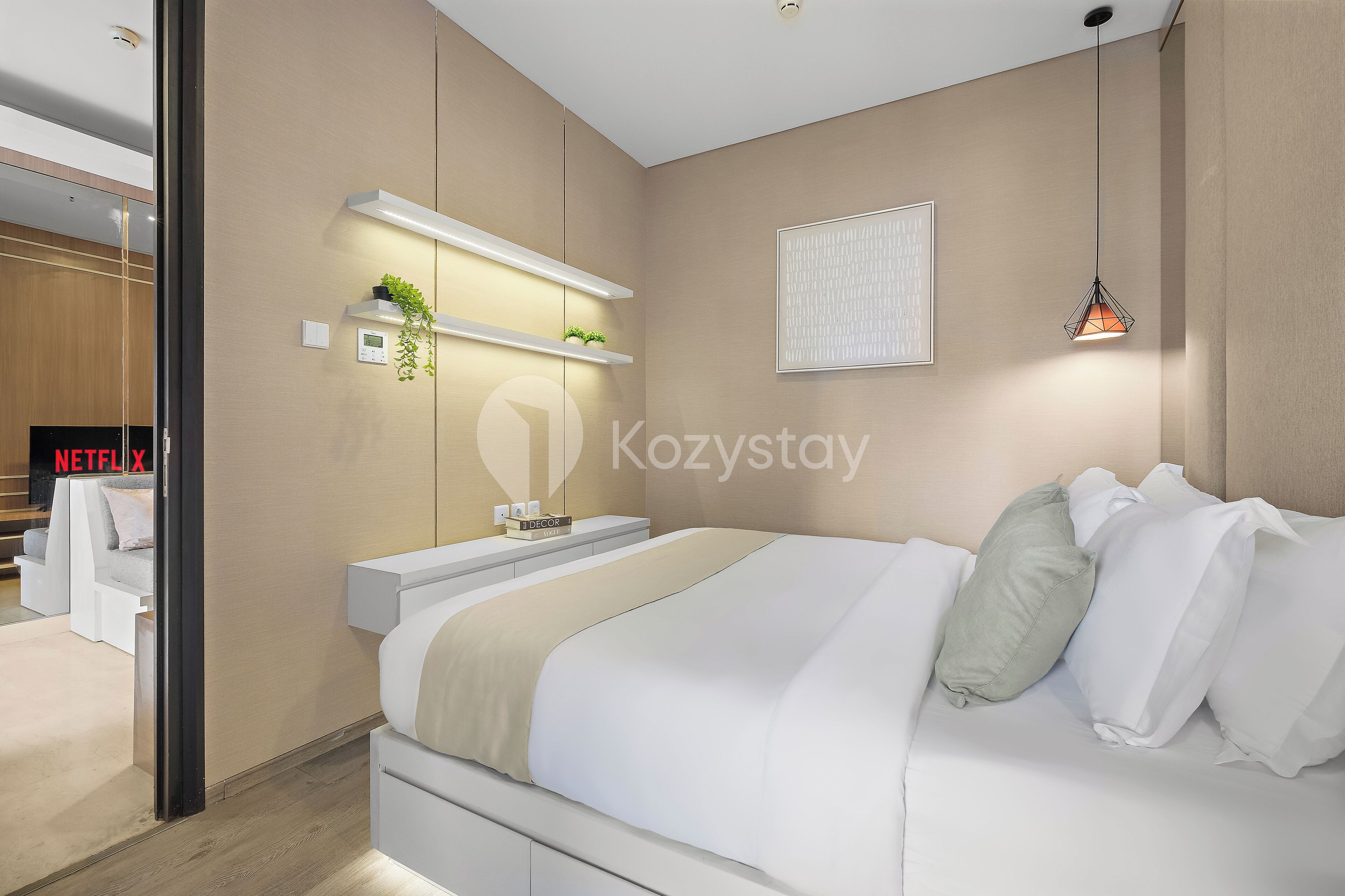 Quarto de hotel moderno com cama, mesas de cabeceira, prateleira com plantas, uma obra de arte emoldurada e luminária pendente.