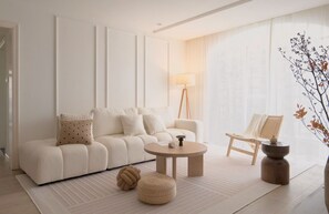 Uma sala de estar moderna com sofá, mesa de centro redonda, mesa lateral, luminária de chão e uma poltrona.