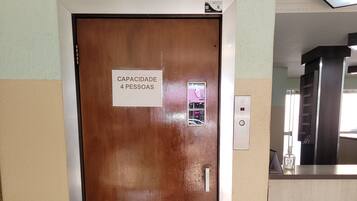 Porta de elevador de madeira com sinal indicando capacidade para 4 pessoas.