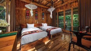 Quarto com decoração em madeira, duas camas, uma mesa de jantar e vista para área verde.