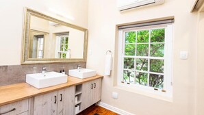 Casa de banho com duas pias, um espelho grande, janela com vista para árvores e chão de madeira.