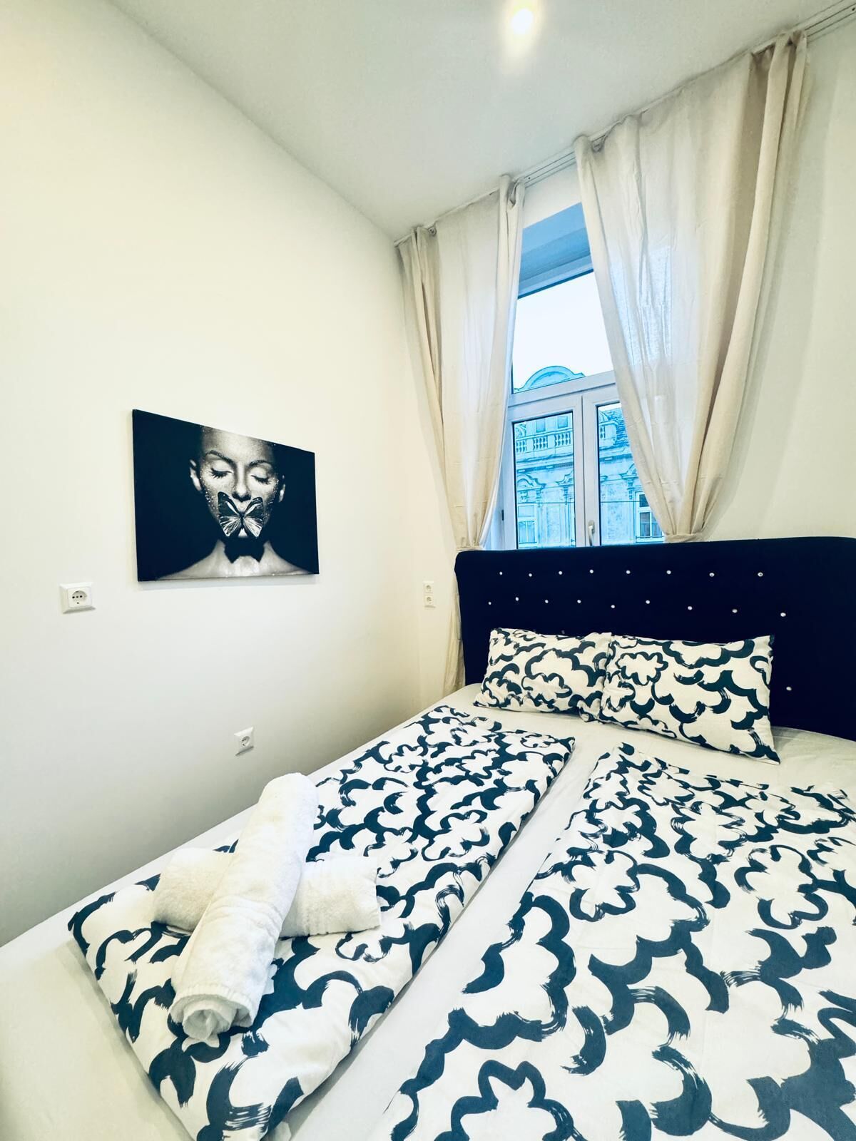 Quarto com cama, cabeceira, janela com cortinas e uma obra de arte na parede.