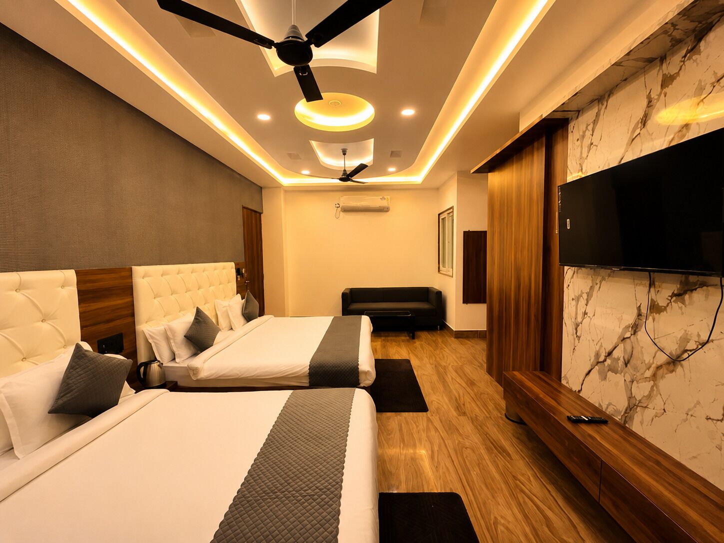 Quarto de hotel com duas camas, um ventilador de teto, iluminação embutida, uma televisão de tela plana e parede com padrão marmorizado.