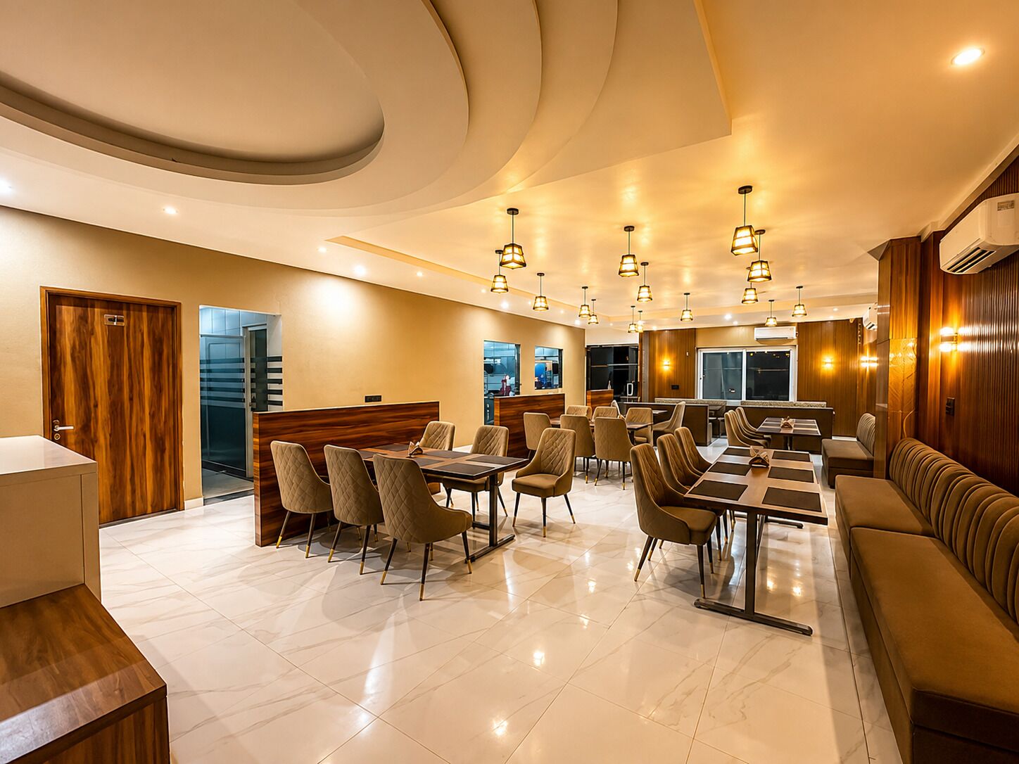 Um espaço de refeições moderno em hotel, com uma mesa comunitária grande, mesas individuais e uma área de estar com sofás.