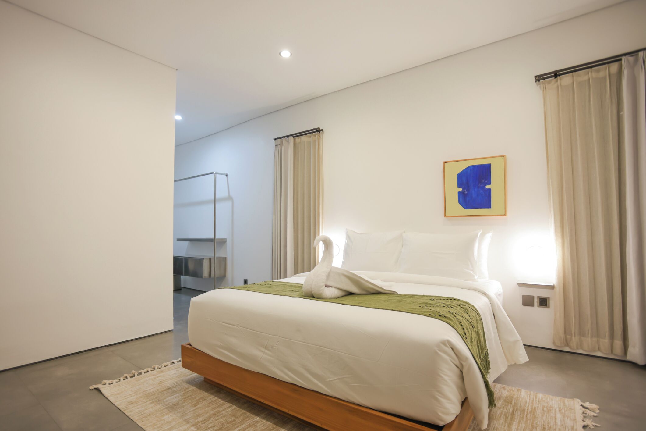 Quarto moderno com uma cama grande, um cobertor verde e uma pintura abstrata azul na parede.