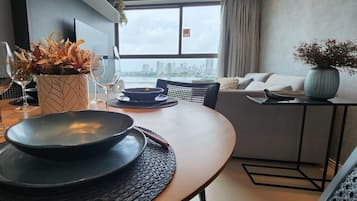 Uma sala de jantar moderna com vista para a cidade, um sofá e uma mesa posta com pratos, tigelas e copos de vinho.