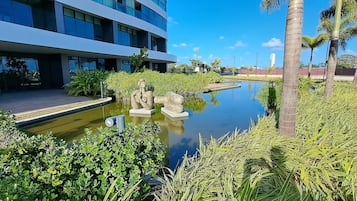 Um edifício moderno com uma piscina refletora, rodeado por vegetação exuberante e palmeiras.