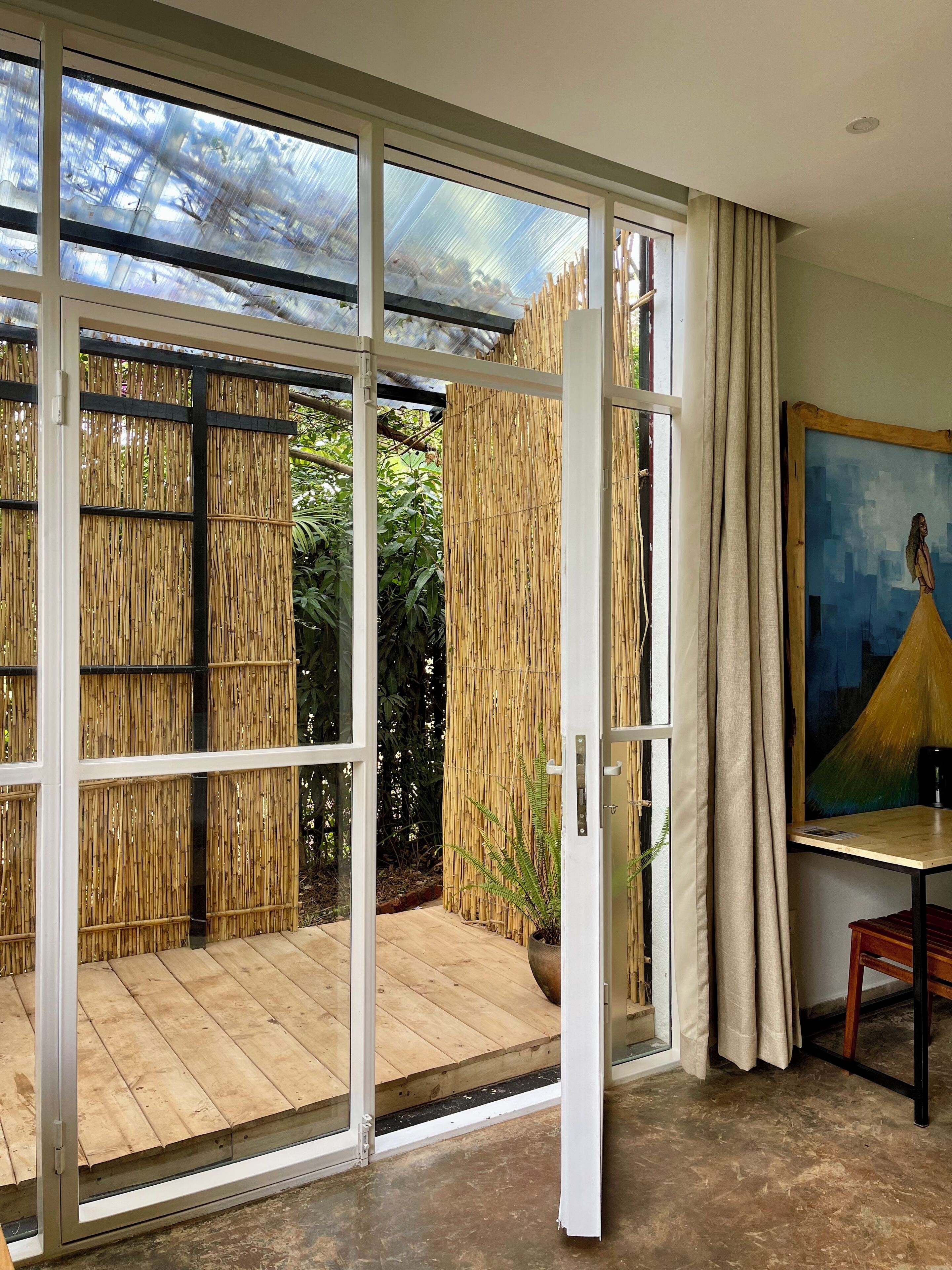 Quarto com porta de vidro deslizante que dá para área externa com cerca de bambu e deck de madeira.