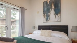 Quarto com uma cama grande, vista pela porta de correr, um quadro na parede e um abajur na mesinha de cabeceira.
