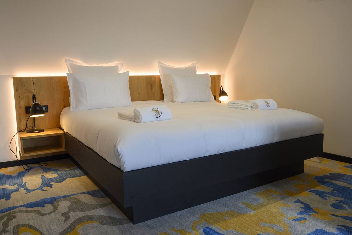 Quarto de hotel moderno com uma cama grande, cabeceira de madeira, luminárias de cabeceira e um tapete estampado.