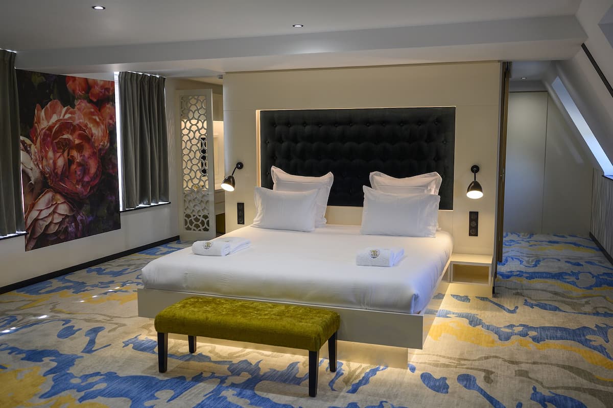 Quarto de hotel moderno com uma cama grande, um banco e um detalhe decorativo na parede.
