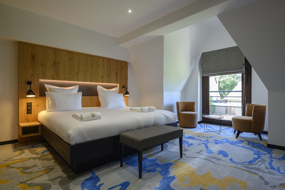 Quarto moderno com uma cama grande, um banquinho, duas cadeiras e uma janela com vista.