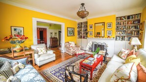 Uma sala de estar com sofá, poltronas, uma mesa de centro e uma estante cheia de livros.