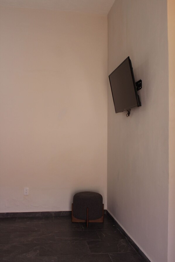 Quarto com piso escuro, um banquinho redondo pequeno, TV fixada na parede e uma tomada.