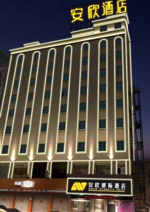 Um edifício de hotel com vários andares, uma placa chamativa no topo e uma placa de identificação na entrada.