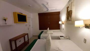 Quarto de hotel com duas camas, televisão, escrivaninha e luminária na parede.