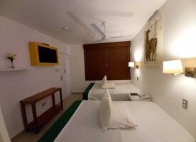 Quarto de hotel com duas camas, televisão, escrivaninha e luminária na parede.