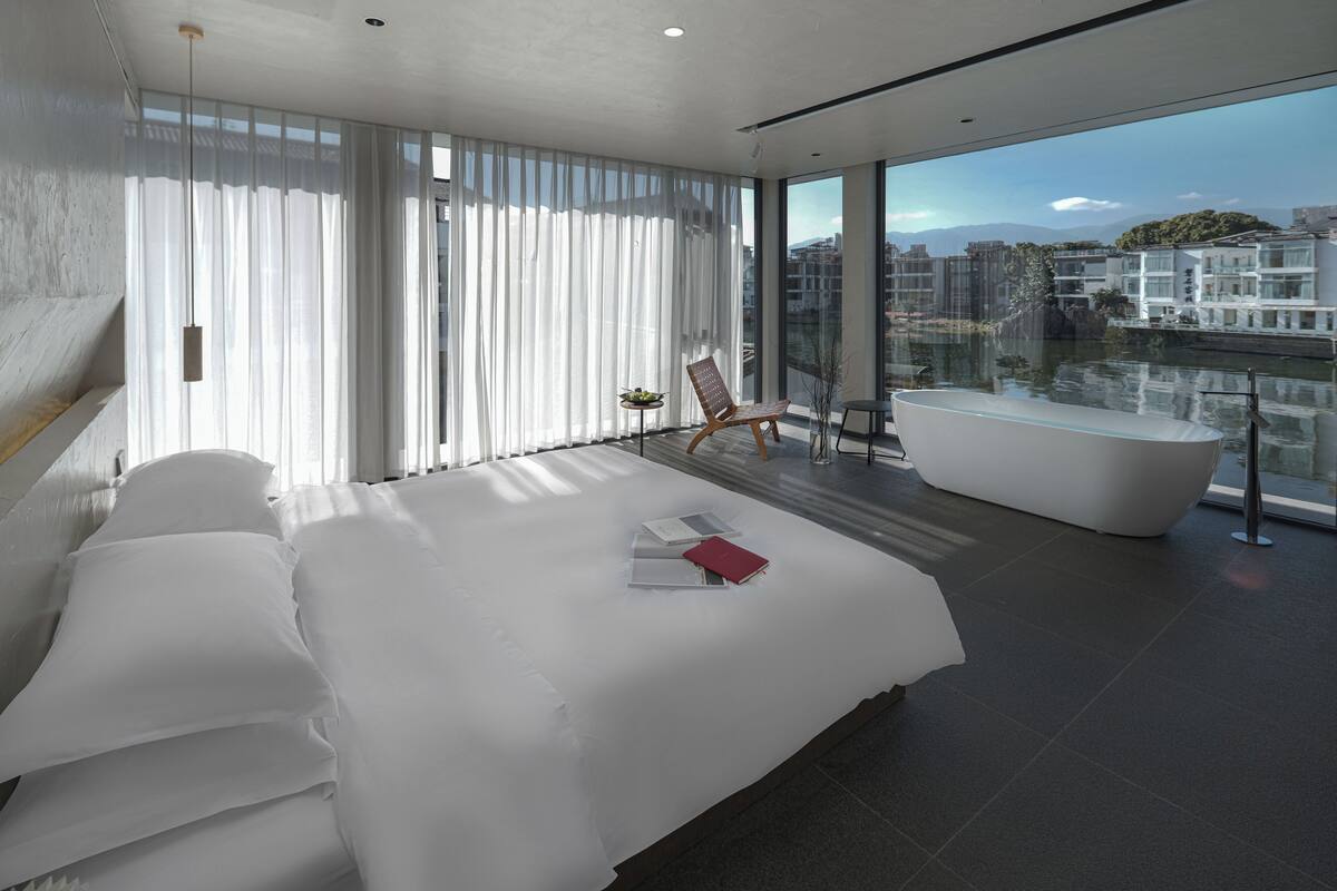 Quarto de hotel moderno com uma cama grande, vista da cidade e varanda privativa com banheira.