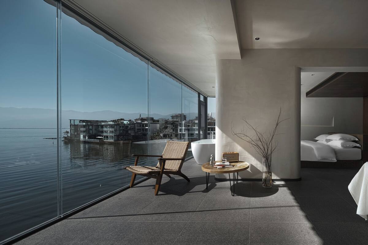 Quarto de hotel moderno com uma varanda grande com vista para um corpo de água e para o horizonte urbano.