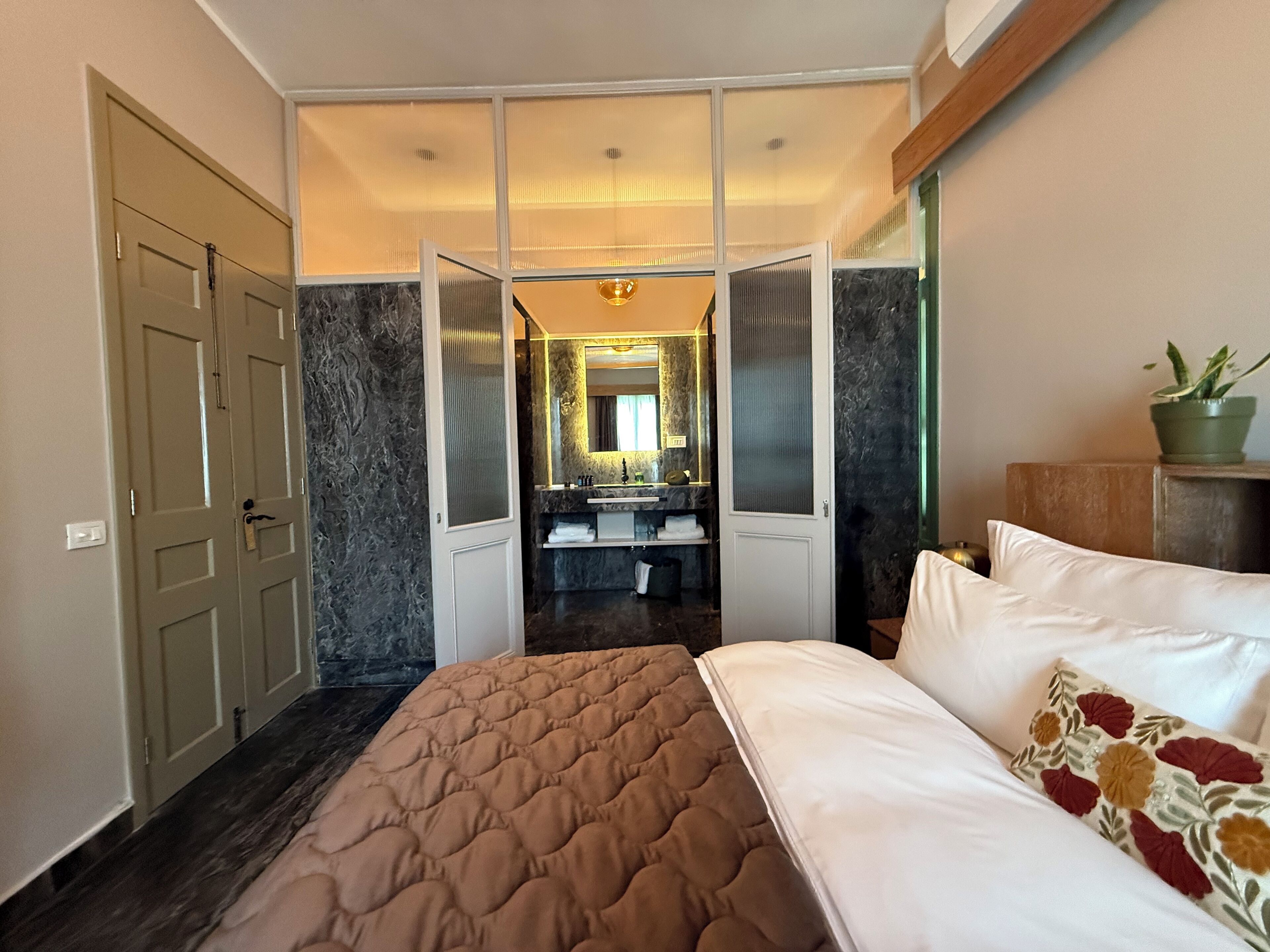 Quarto com cama, banheiro com espelho e pia, e corredor que leva a um banheiro.