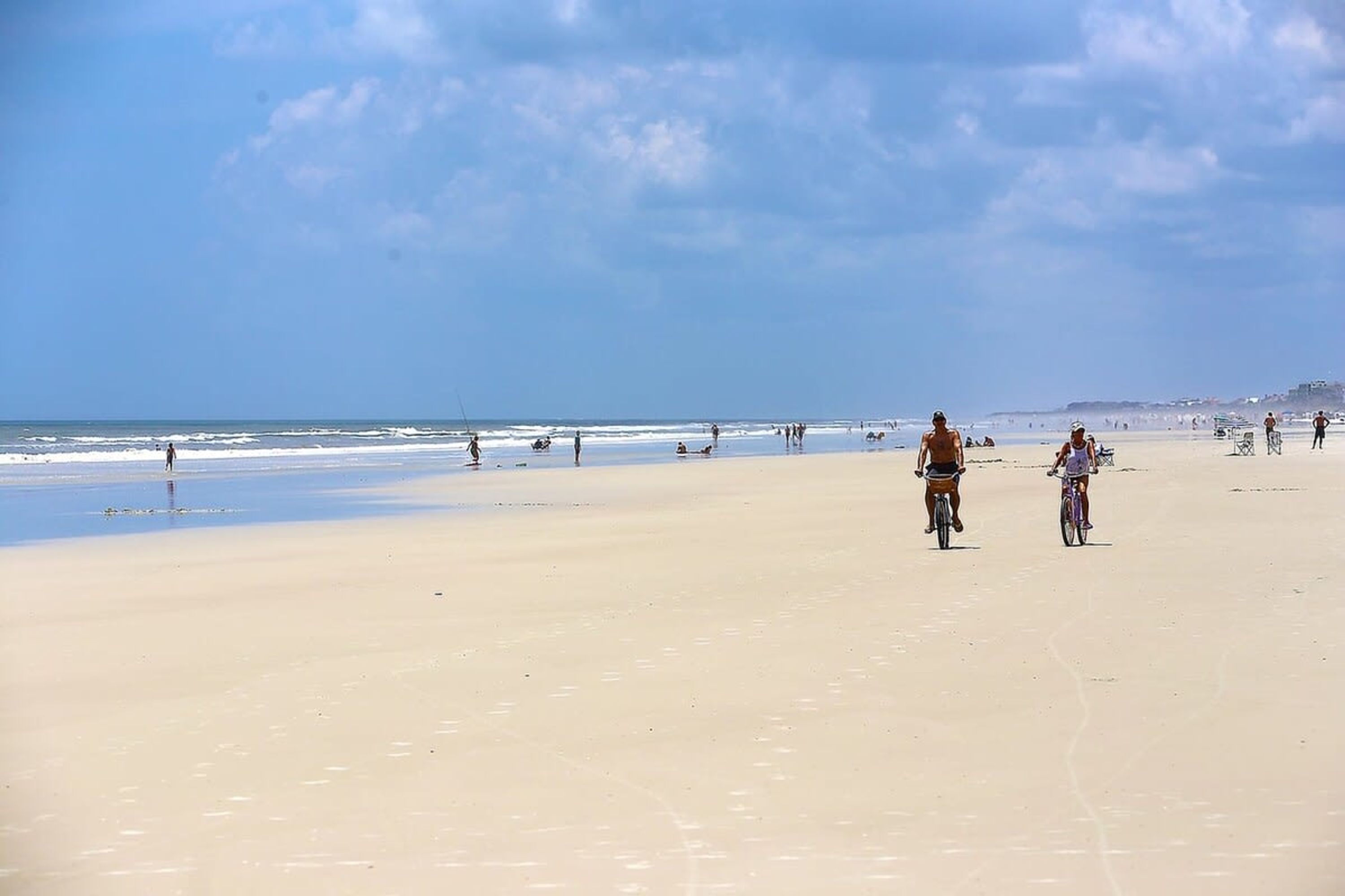 Uma extensa praia de areia com pessoas caminhando e andando de bicicleta.