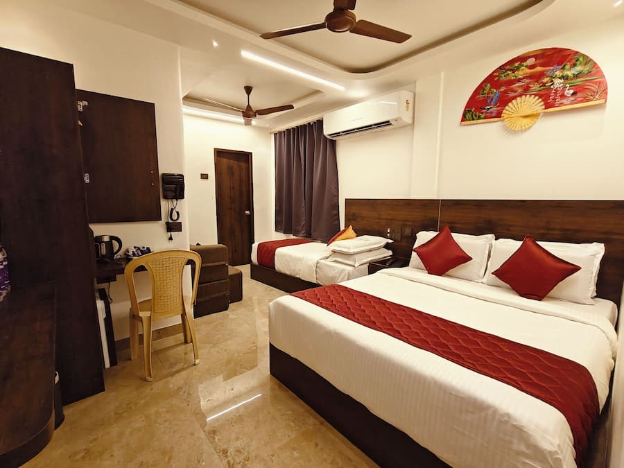 Quarto de hotel com duas camas, uma escrivaninha, uma cadeira, ar condicionado e um ventilador de teto, além de um objeto decorativo na parede.