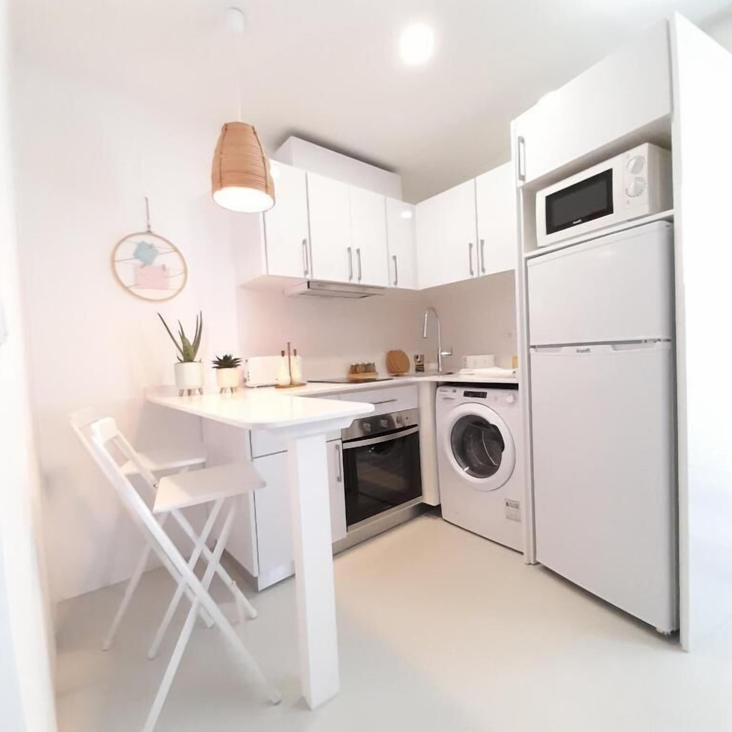 Uma cozinha moderna com armários brancos, forno embutido, máquina de lavar e micro-ondas.