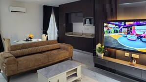 Uma sala de estar moderna com um sofá marrom, uma mesinha de centro, uma televisão e uma área de cozinha com micro-ondas.