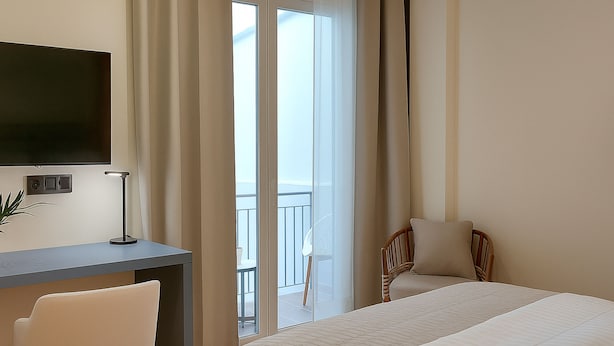 Quarto de hotel com cama, escrivaninha com cadeira, televisão e varanda com uma cadeira.