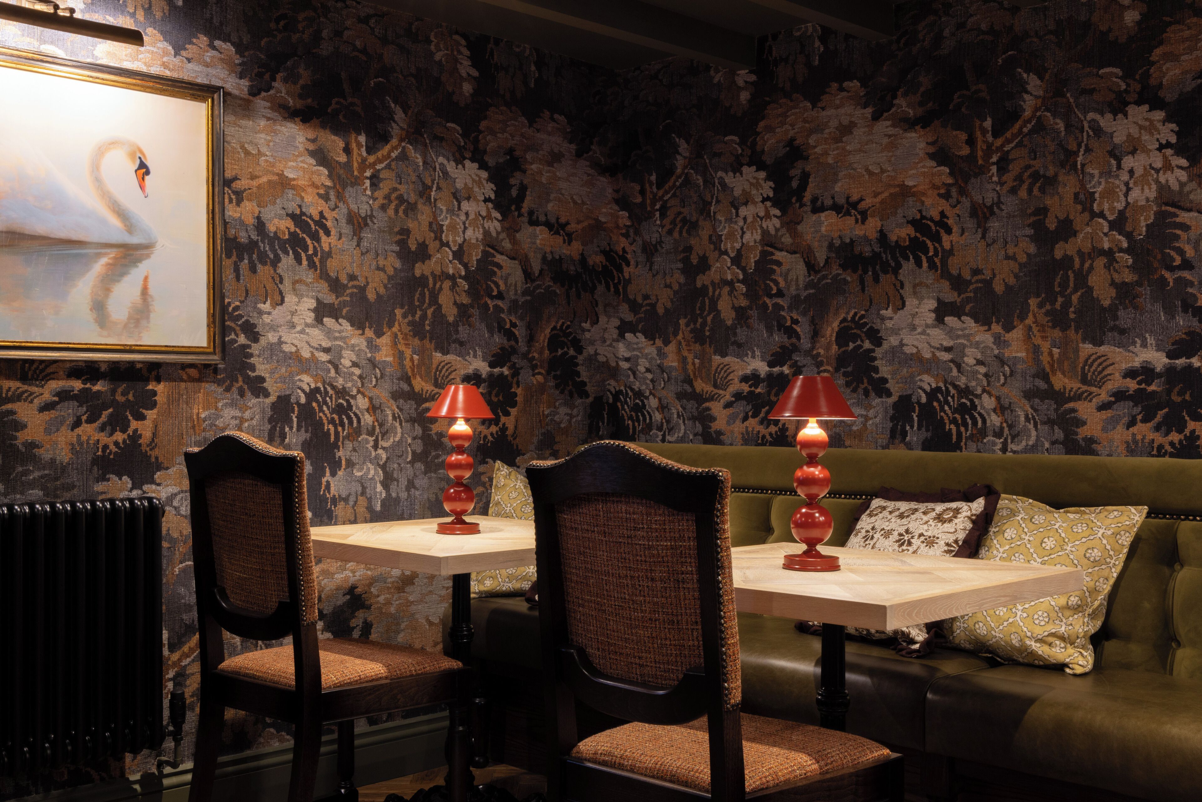 Uma sala de jantar com um sofá verde, duas cadeiras, uma mesa e duas luminárias vermelhas.