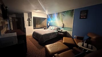 Quarto de hotel com cama, escrivaninha, cadeira, mesinha e um mural na parede com uma cena de praia.