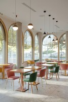 Interior moderno de restaurante com grandes janelas em arco, várias mesas e cadeiras, e iluminação pendente.