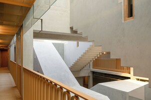 Um interior moderno com uma escada que leva a um andar superior, corrimão de madeira e parede de concreto.