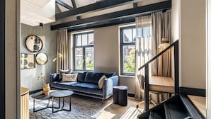 Uma sala de estar moderna com um sofá azul, uma mesa de centro redonda e uma escada com acabamento em madeira.