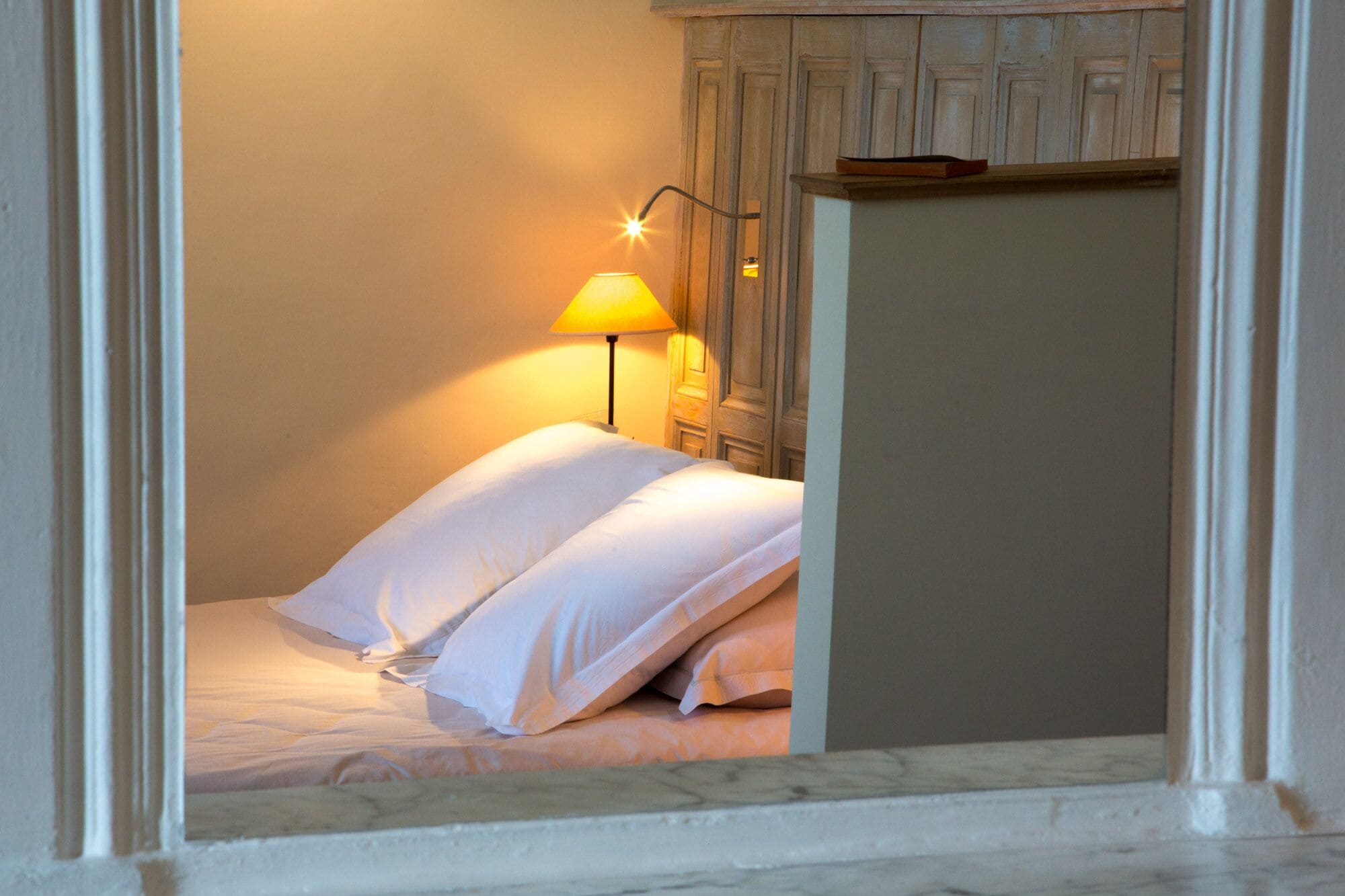 Um quarto com uma cama, travesseiros, mesa de cabeceira e abajur.