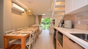 Cozinha moderna com armários brancos, uma mesa de jantar de madeira posta para seis pessoas e vista para o exterior.